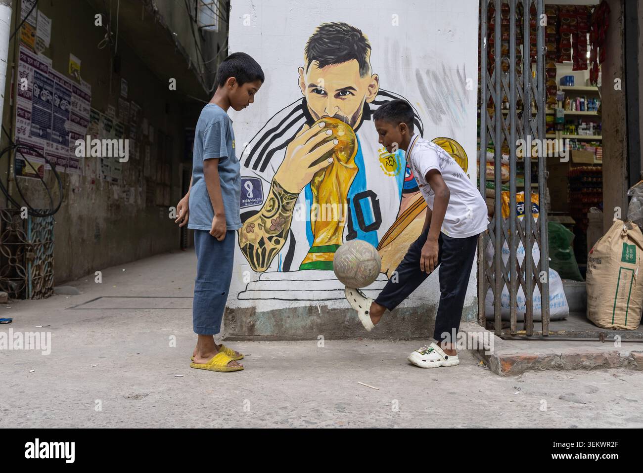 Two boys seen playing foot ball in front of a graffiti of famous ...