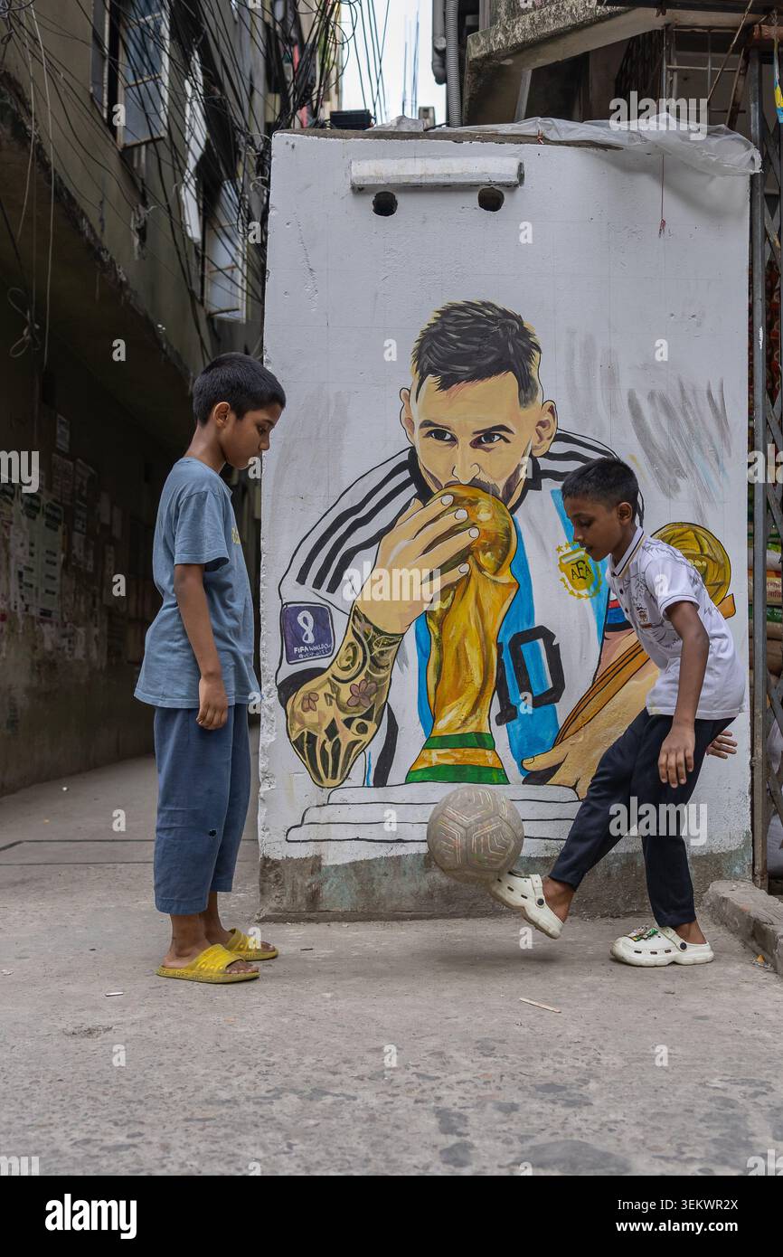 Two boys seen playing foot ball in front of a graffiti of famous ...