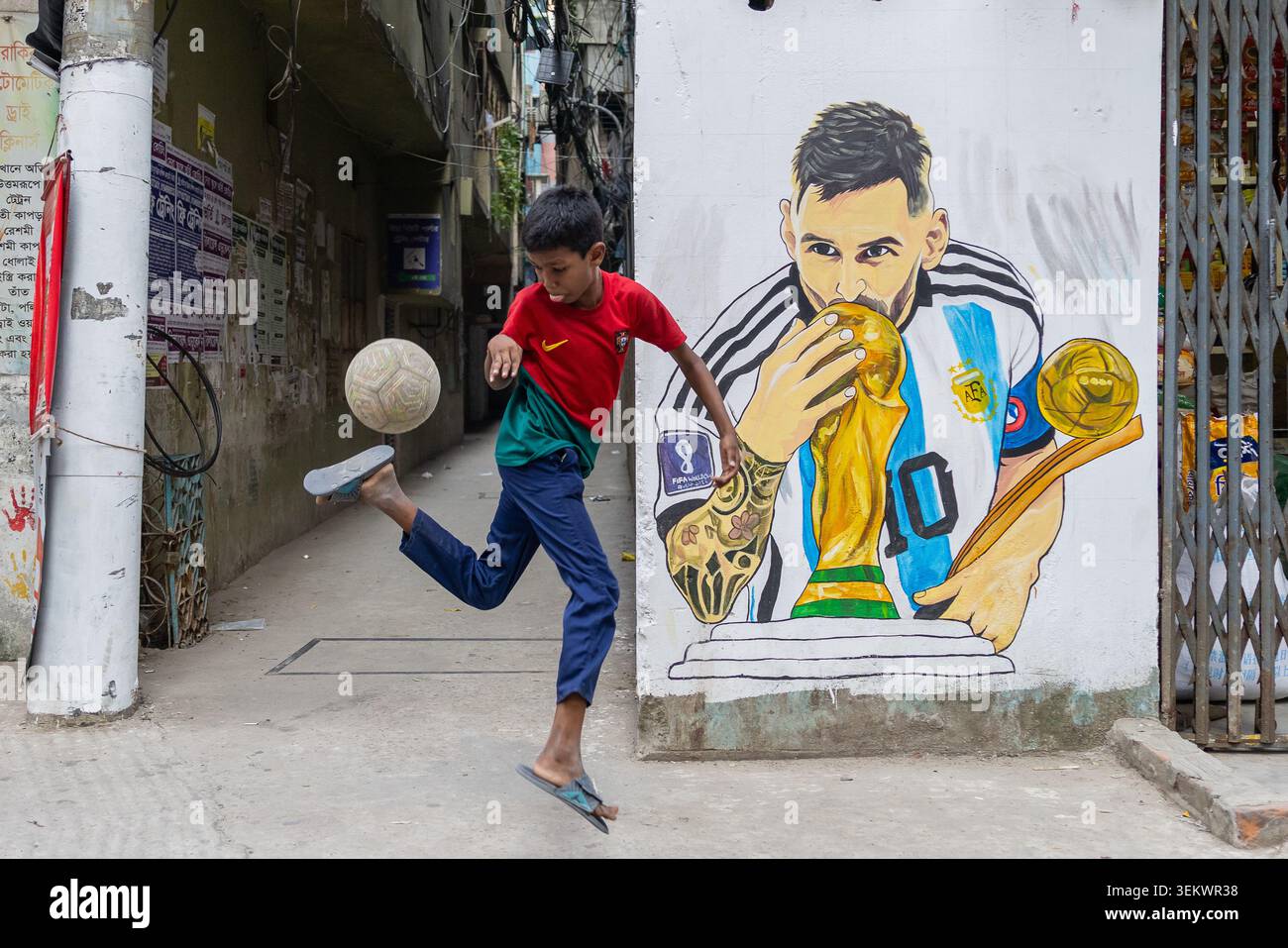 A boy seen playing foot ball in front of a graffiti of famous Argentine ...