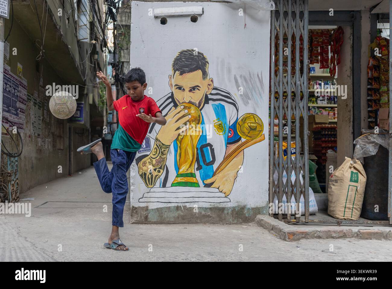 A boy seen playing foot ball in front of a graffiti of famous Argentine ...