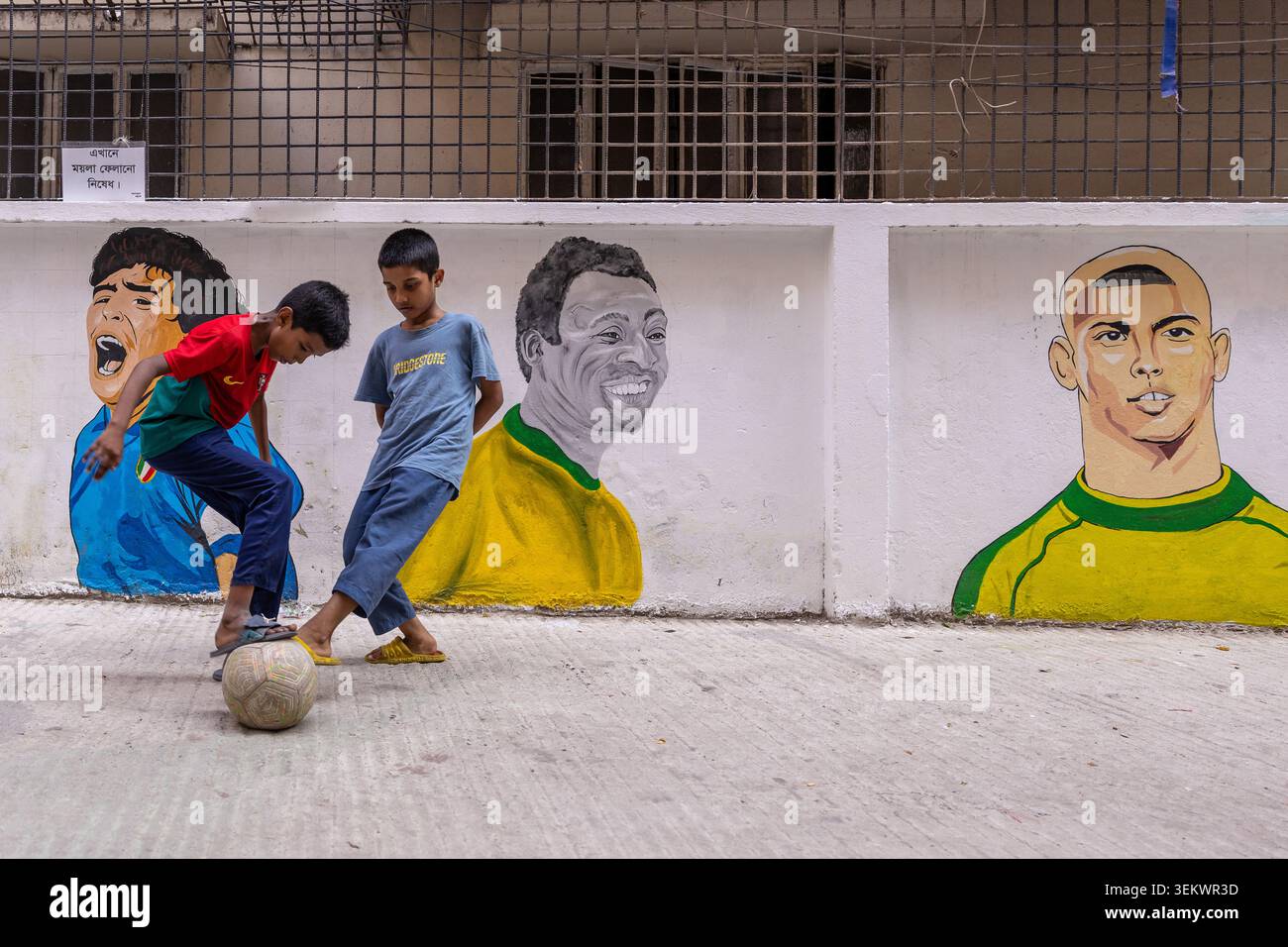 Two boys seen playing foot ball in front of a graffiti of famous ...