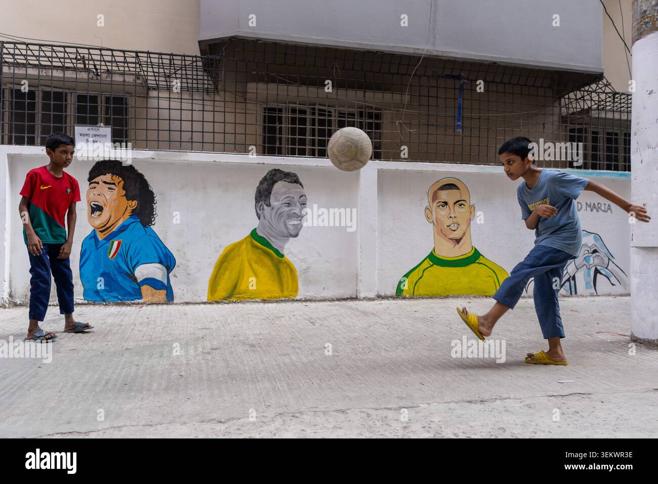 Two boys seen playing foot ball in front of a graffiti of famous ...
