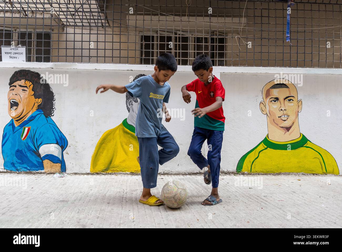 Two boys seen playing foot ball in front of a graffiti of famous ...
