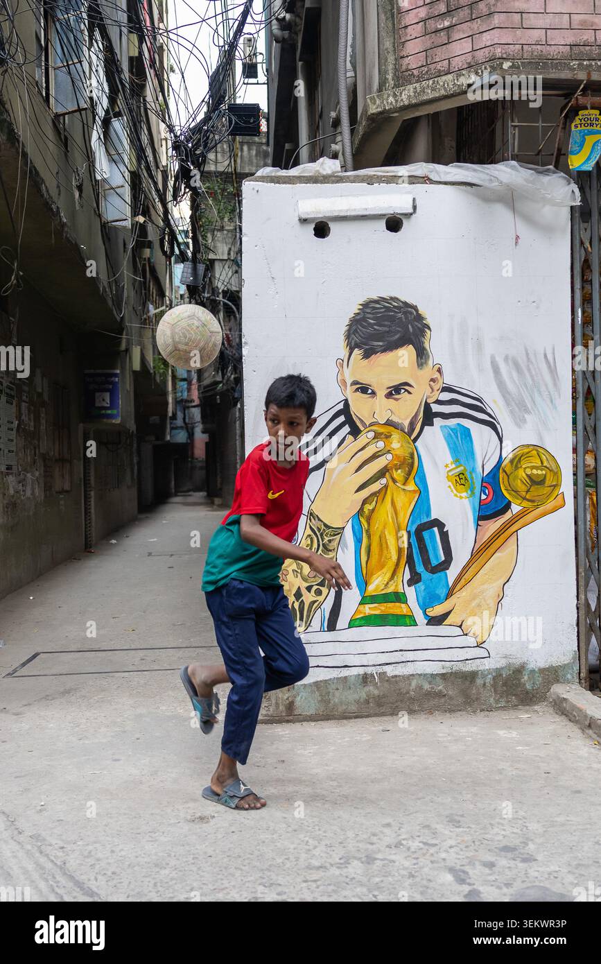 A boy seen playing foot ball in front of a graffiti of famous Argentine ...