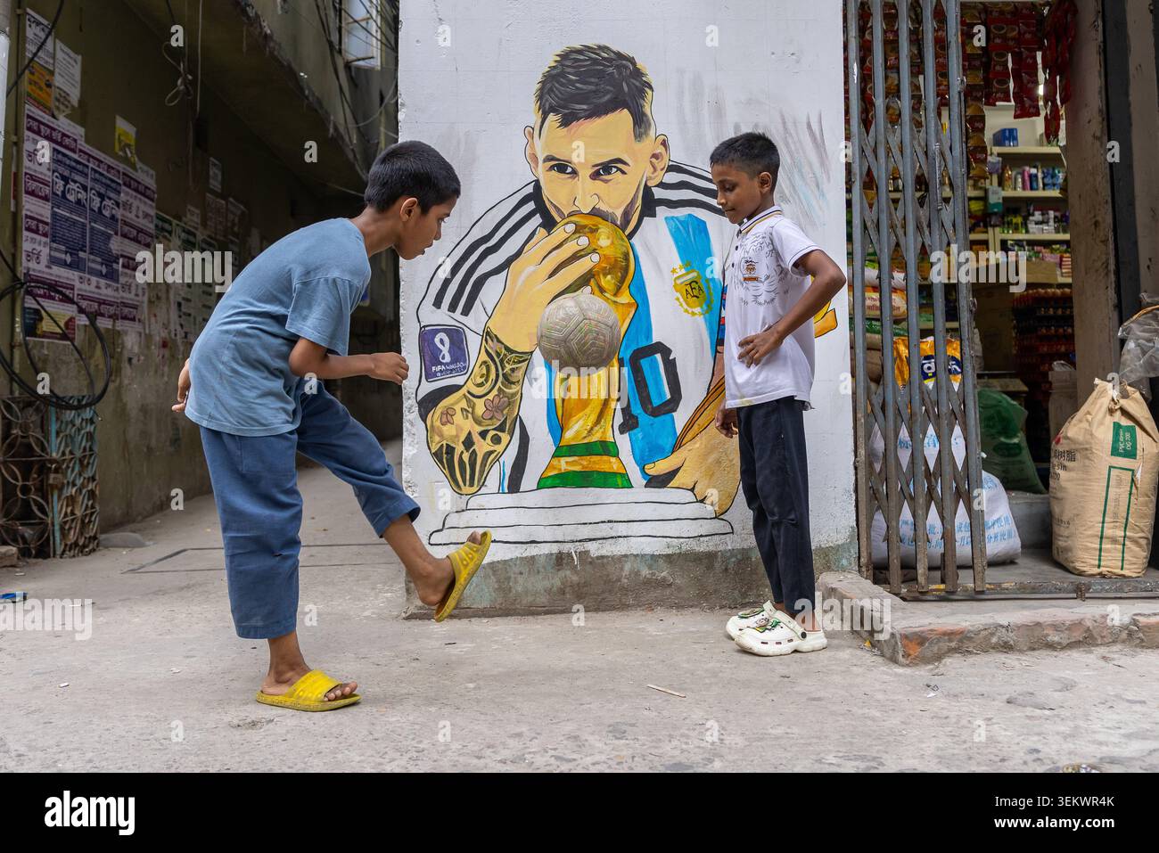 Two boys seen playing foot ball in front of a graffiti of famous ...