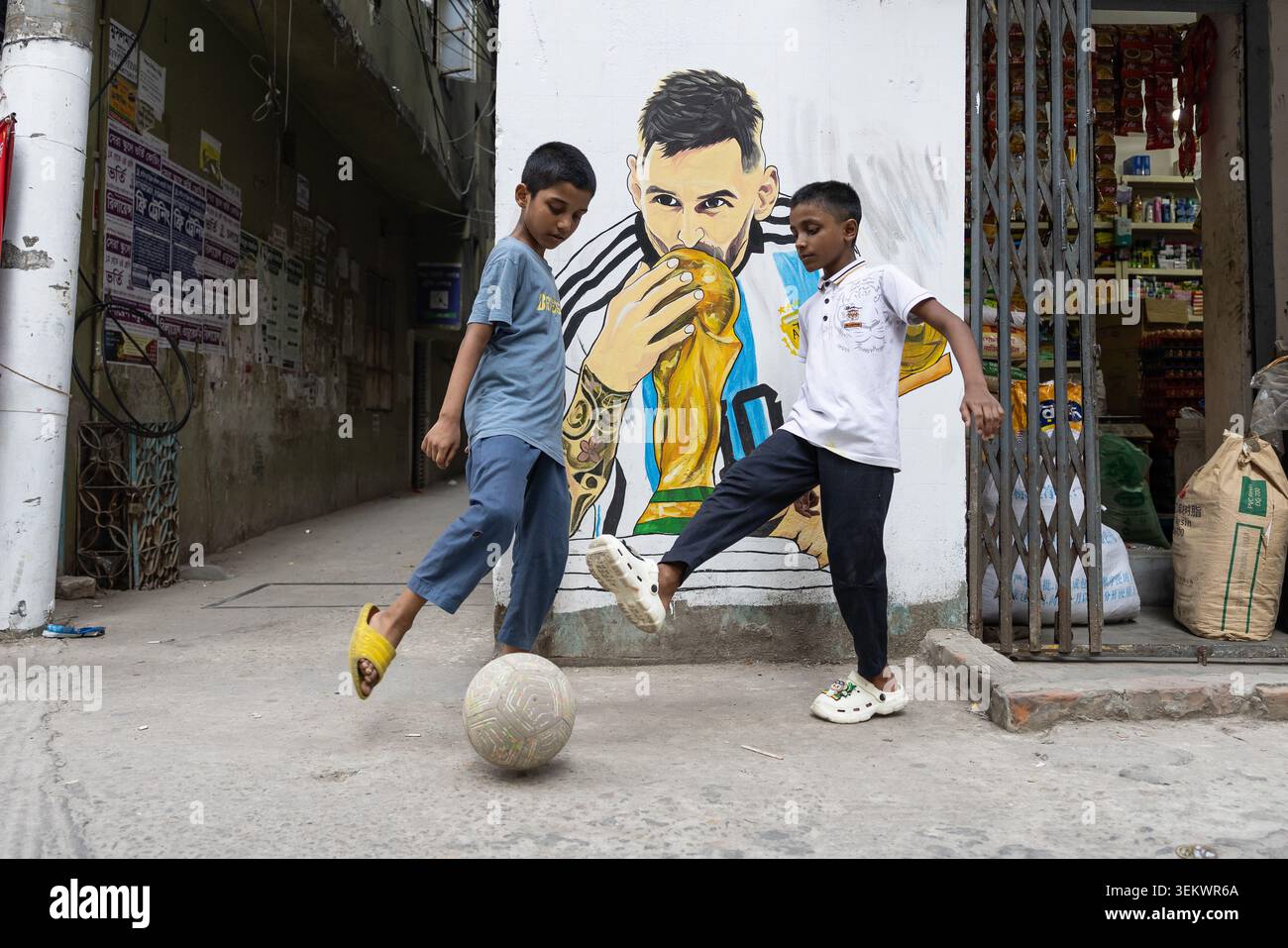 Two boys seen playing foot ball in front of a graffiti of famous ...