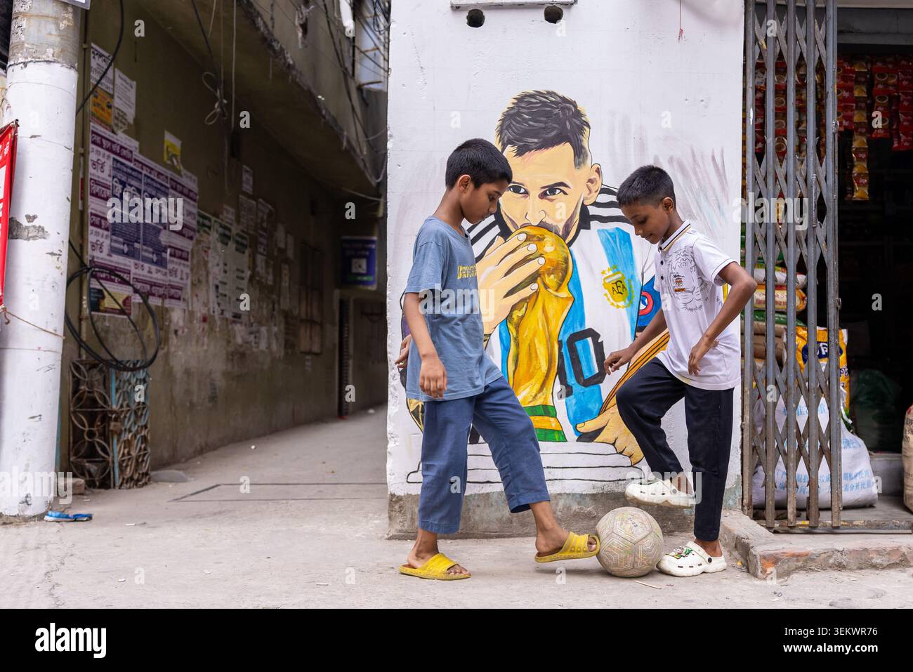 Two boys seen playing foot ball in front of a graffiti of famous ...