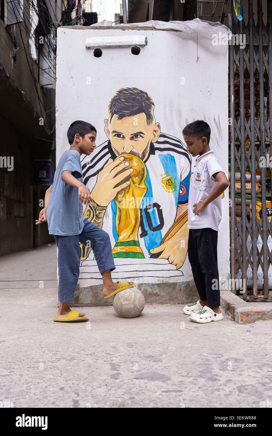 Two boys seen playing foot ball in front of a graffiti of famous ...