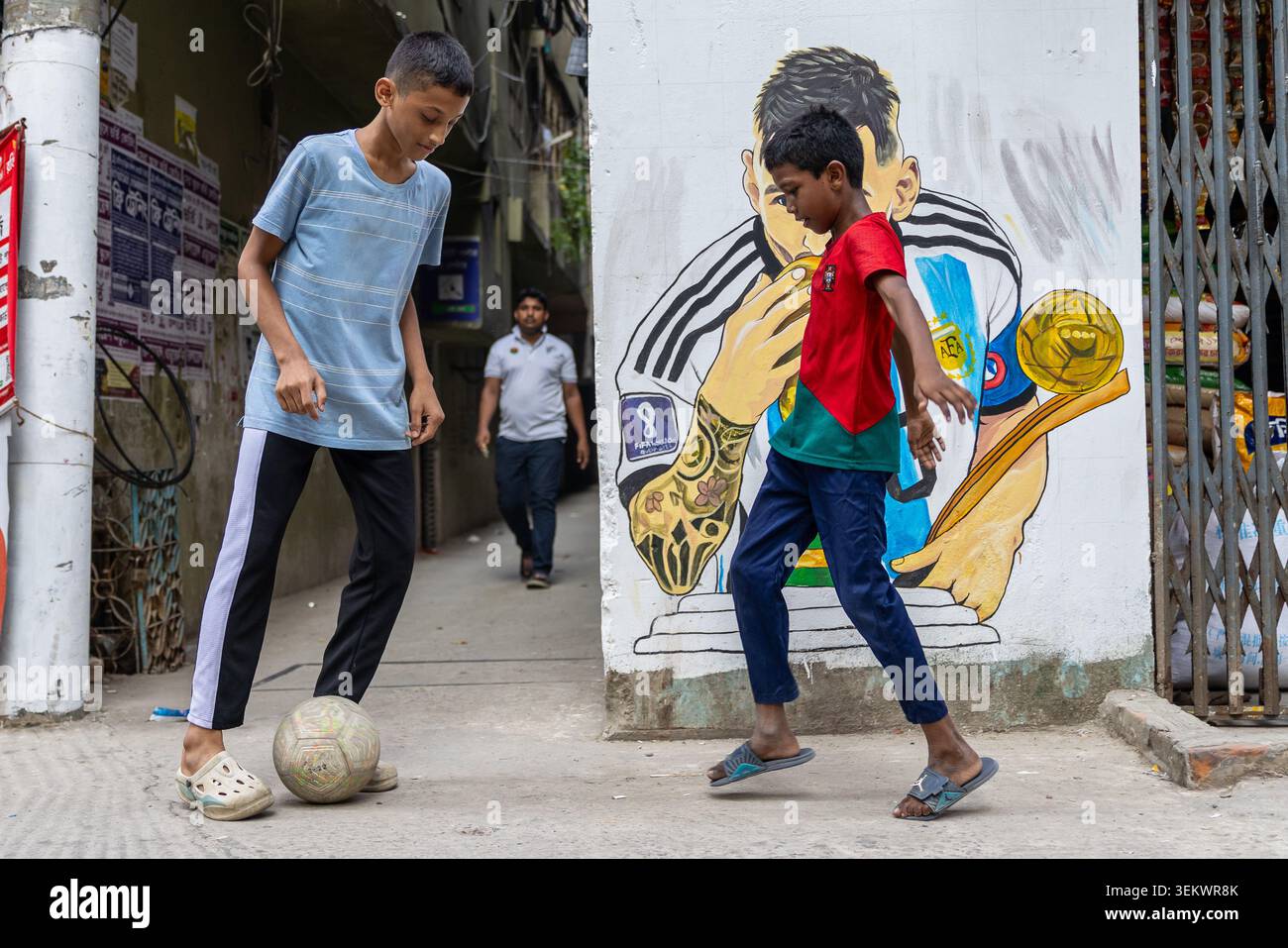 Two boys seen playing foot ball in front of a graffiti of famous ...