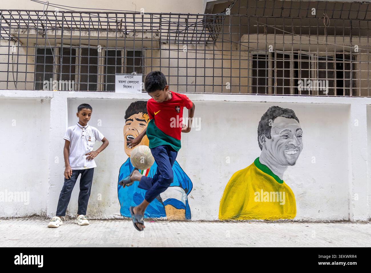 Two boys seen playing foot ball in front of a graffiti of famous ...
