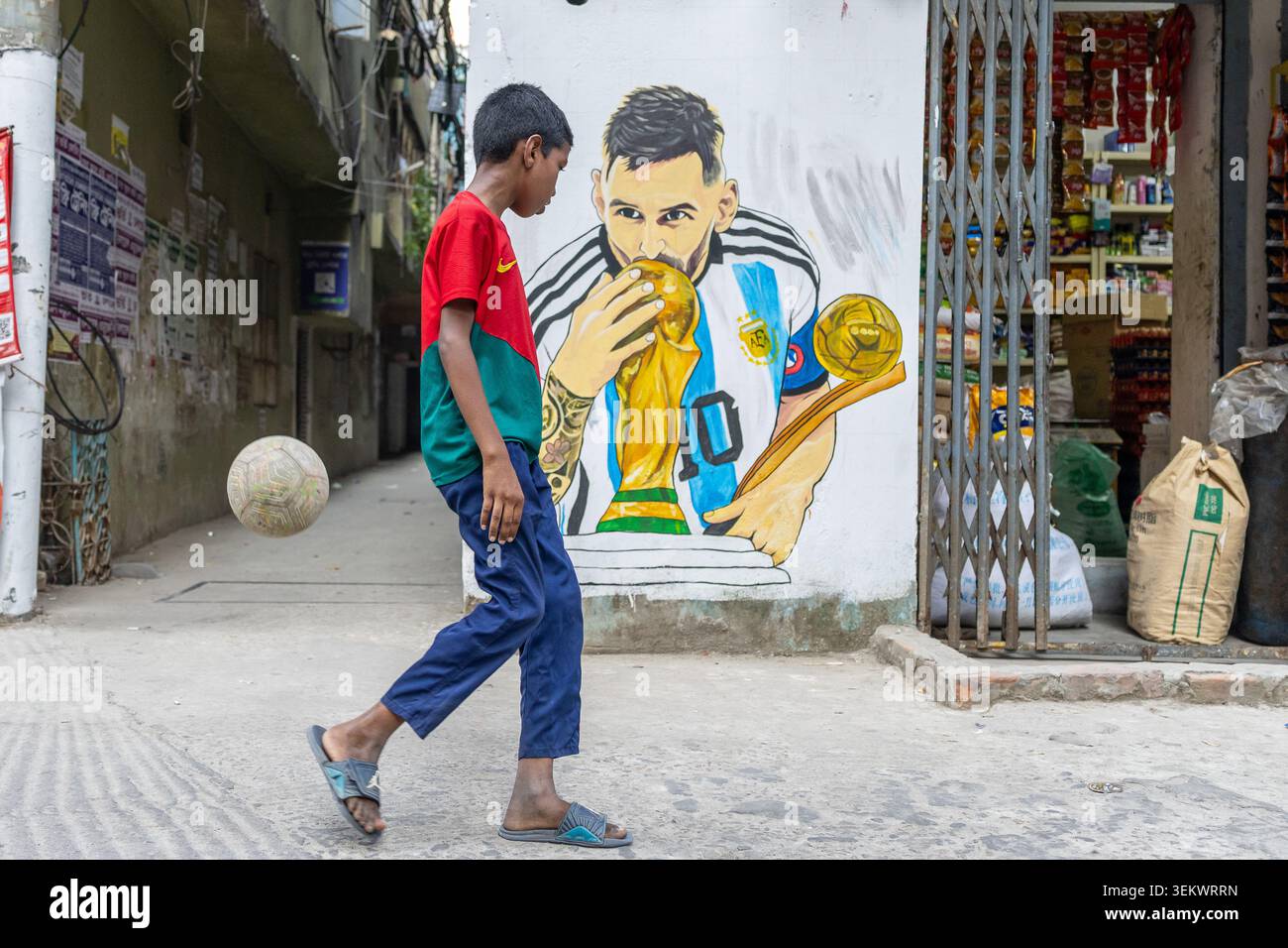 A boy seen playing foot ball in front of a graffiti of famous Argentine ...