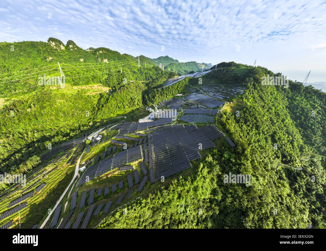 Solar panels stand against green mountains and blue sky at a ...