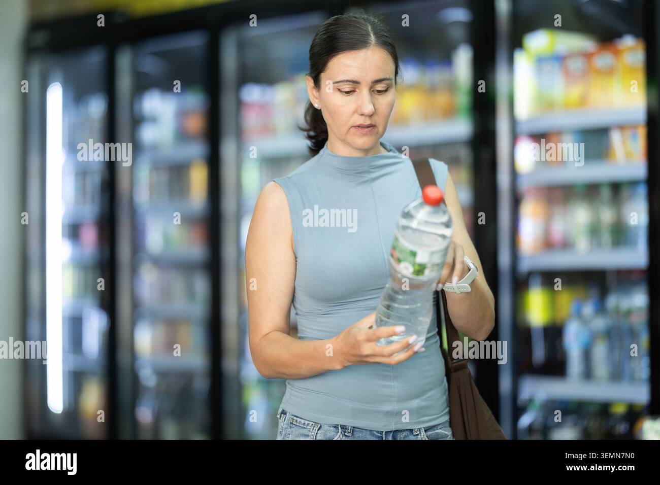 Female customer choosing soft drinks in grocery store, looking at ...