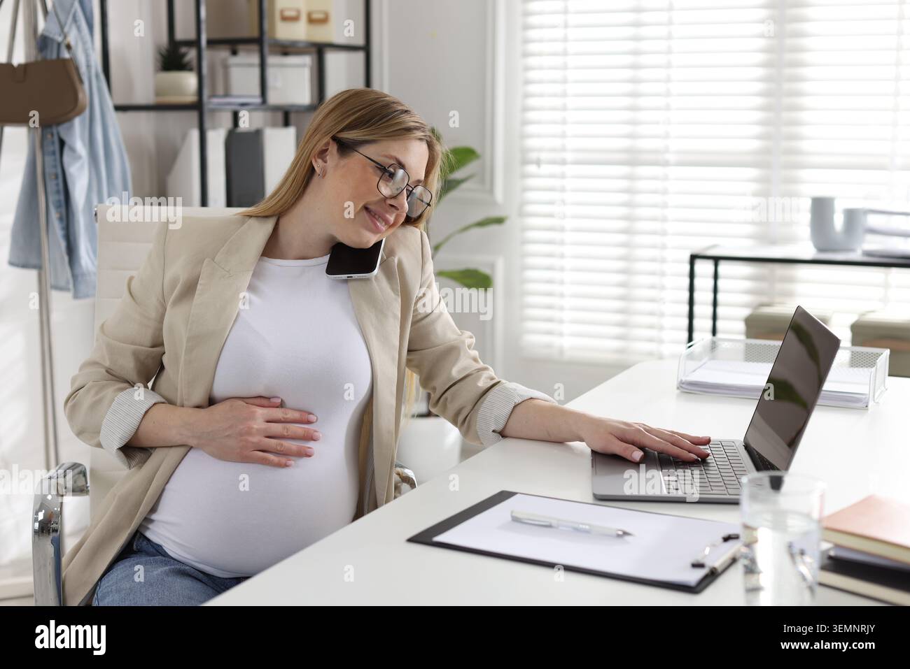 Pregnant woman talking on phone while working with laptop at table ...