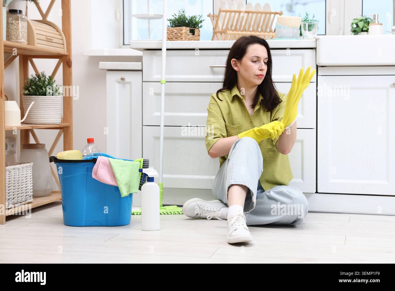 Tired woman with cleaning supplies sitting on floor in kitchen Stock ...