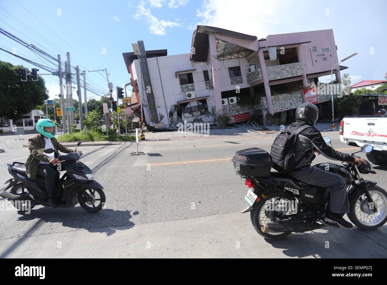 People on motorcycles pass by a collapsed structure after an earthquake ...