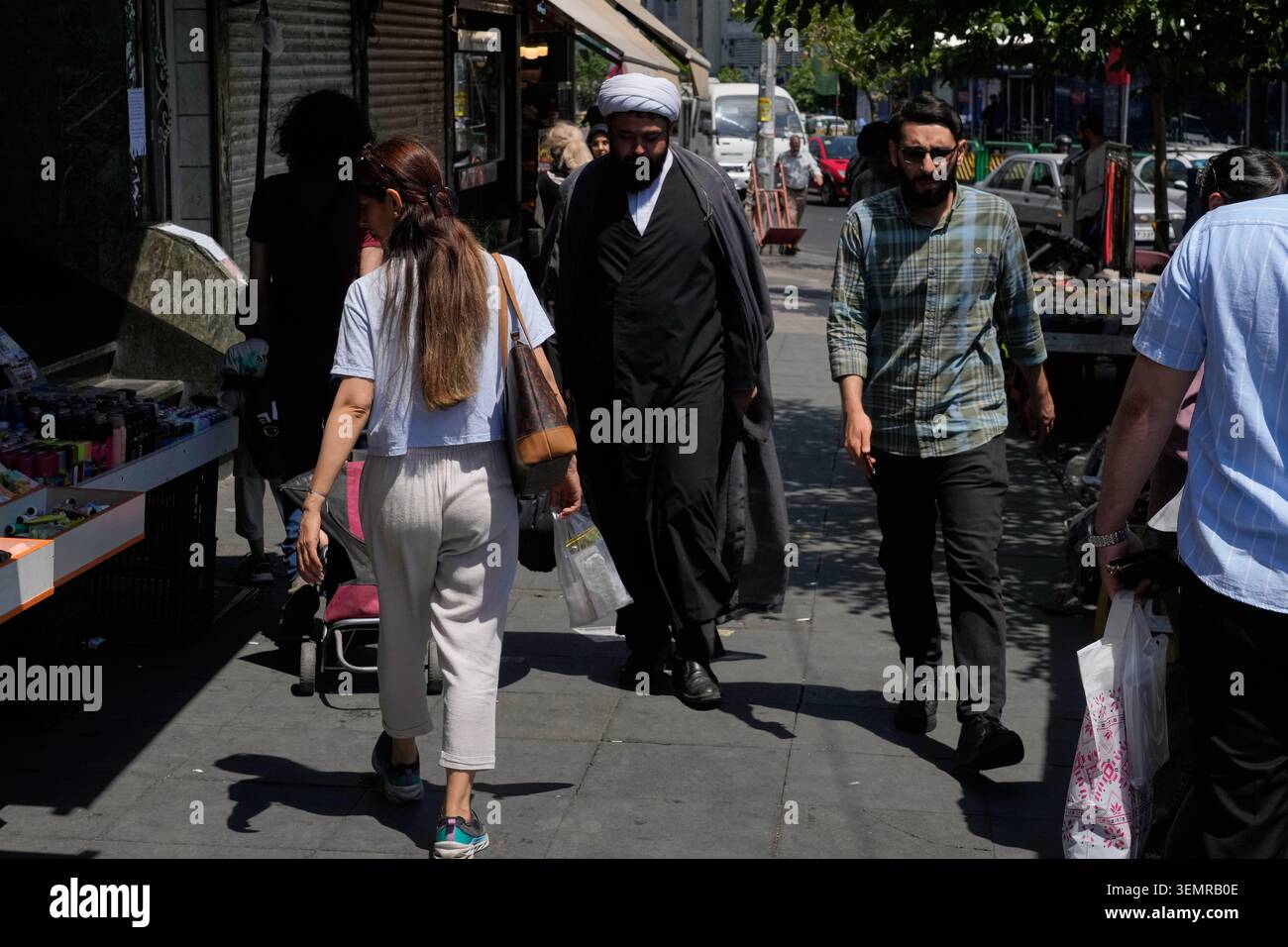 A cleric walks among the other people on a sidewalk at the Islamic ...