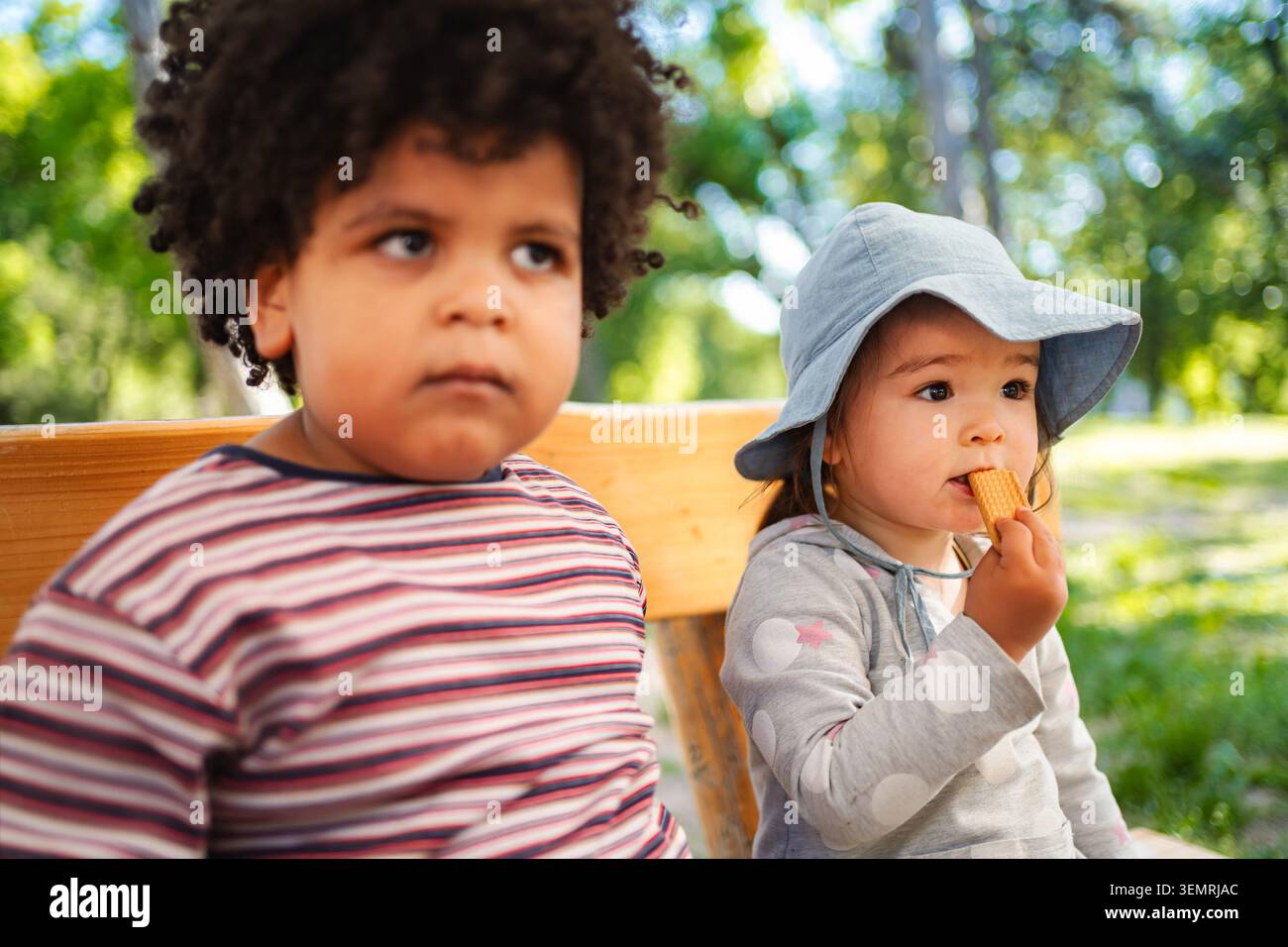 Two young kids sitting outdoors enjoying a snack together in a park ...