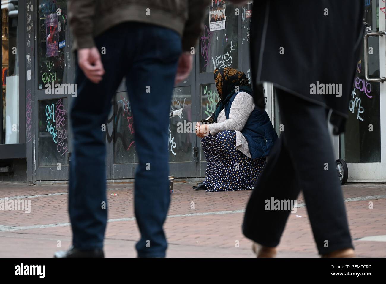 A female beggar sits with a cup against a house wall in the pedestrian ...