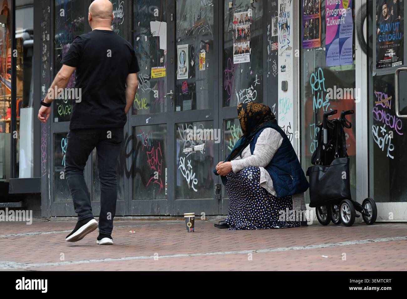 A female beggar sits with a cup against a house wall in the pedestrian ...
