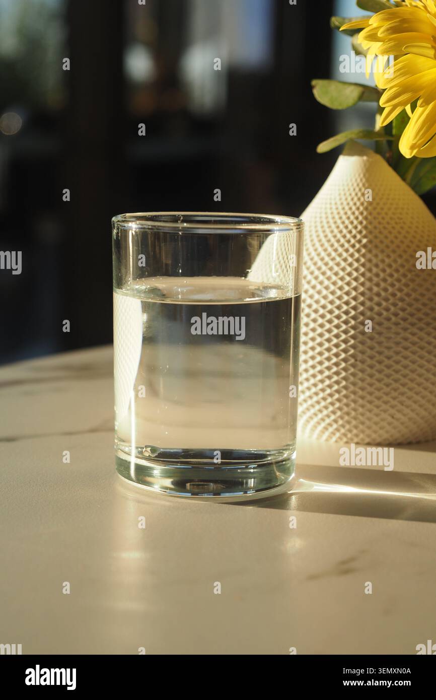 Glass of water next to a vase with yellow flowers Stock Photo - Alamy