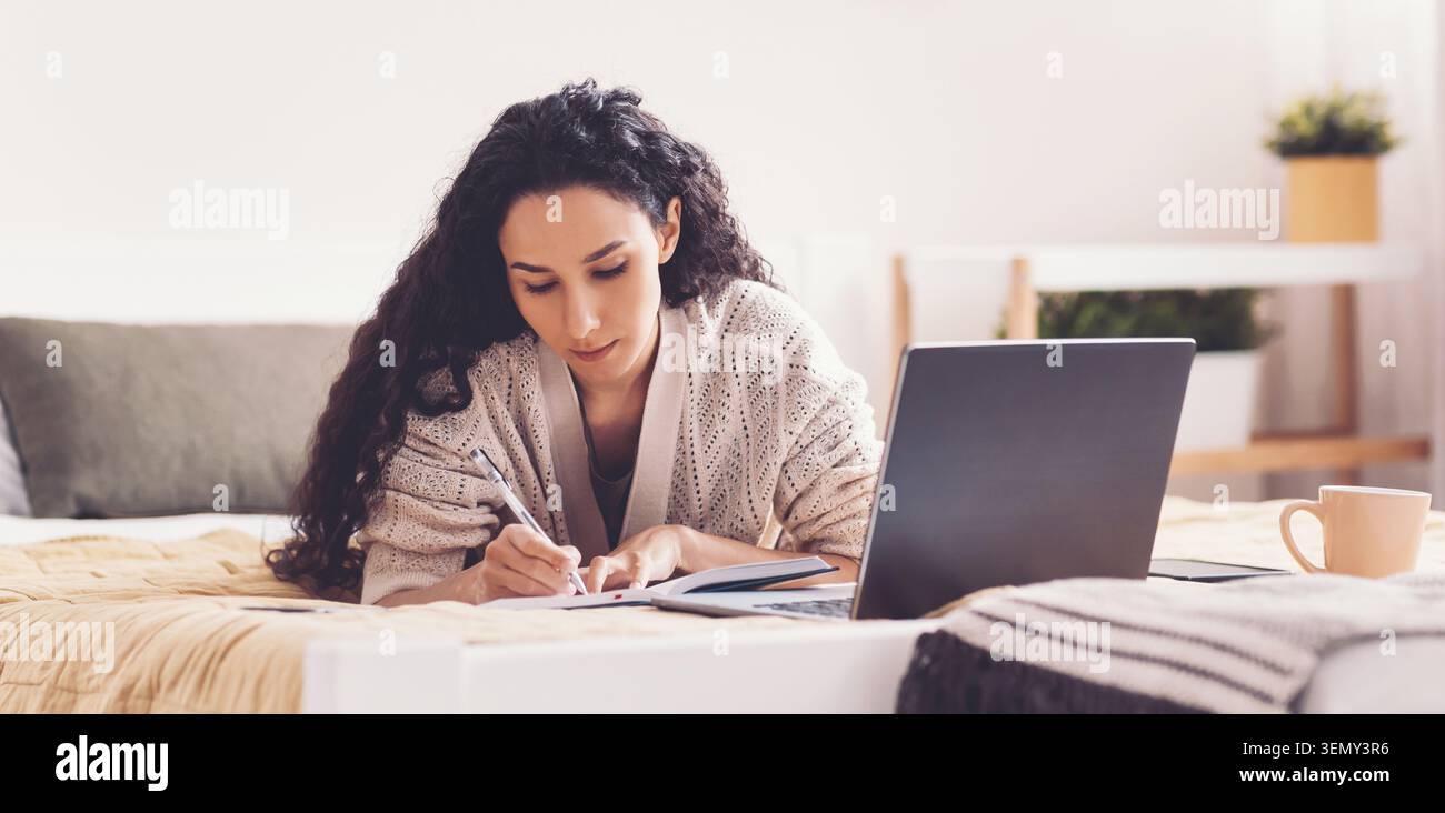 Focused Young Woman Writing In Notebook At Home Office With Laptop ...