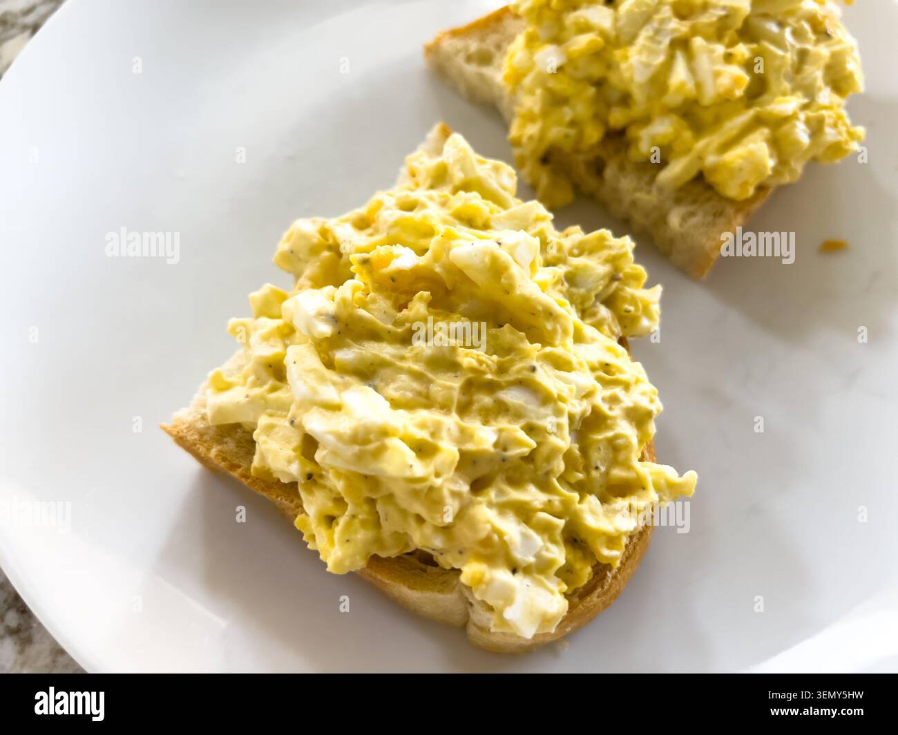 Close-up of a slice of bread generously topped with creamy egg salad ...