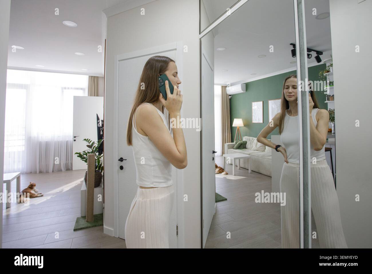 Nice woman looking in the mirror while talking on the phone indoor ...