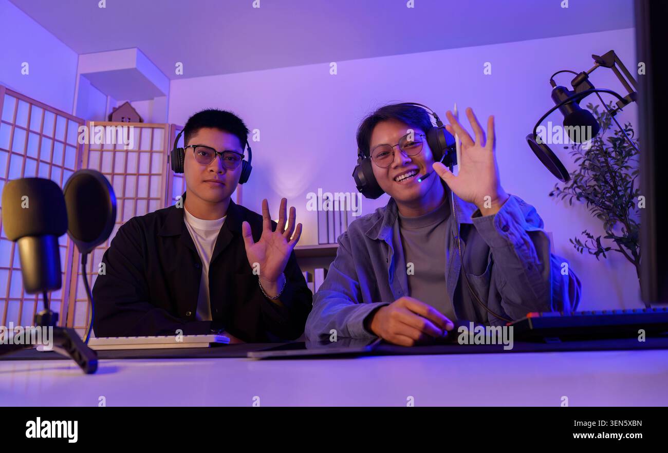 Two Asian men waving at camera while streaming online content with ...