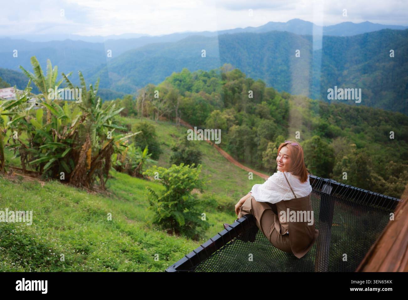 Cheerful woman sitting on glass balcony enjoying beautiful green ...