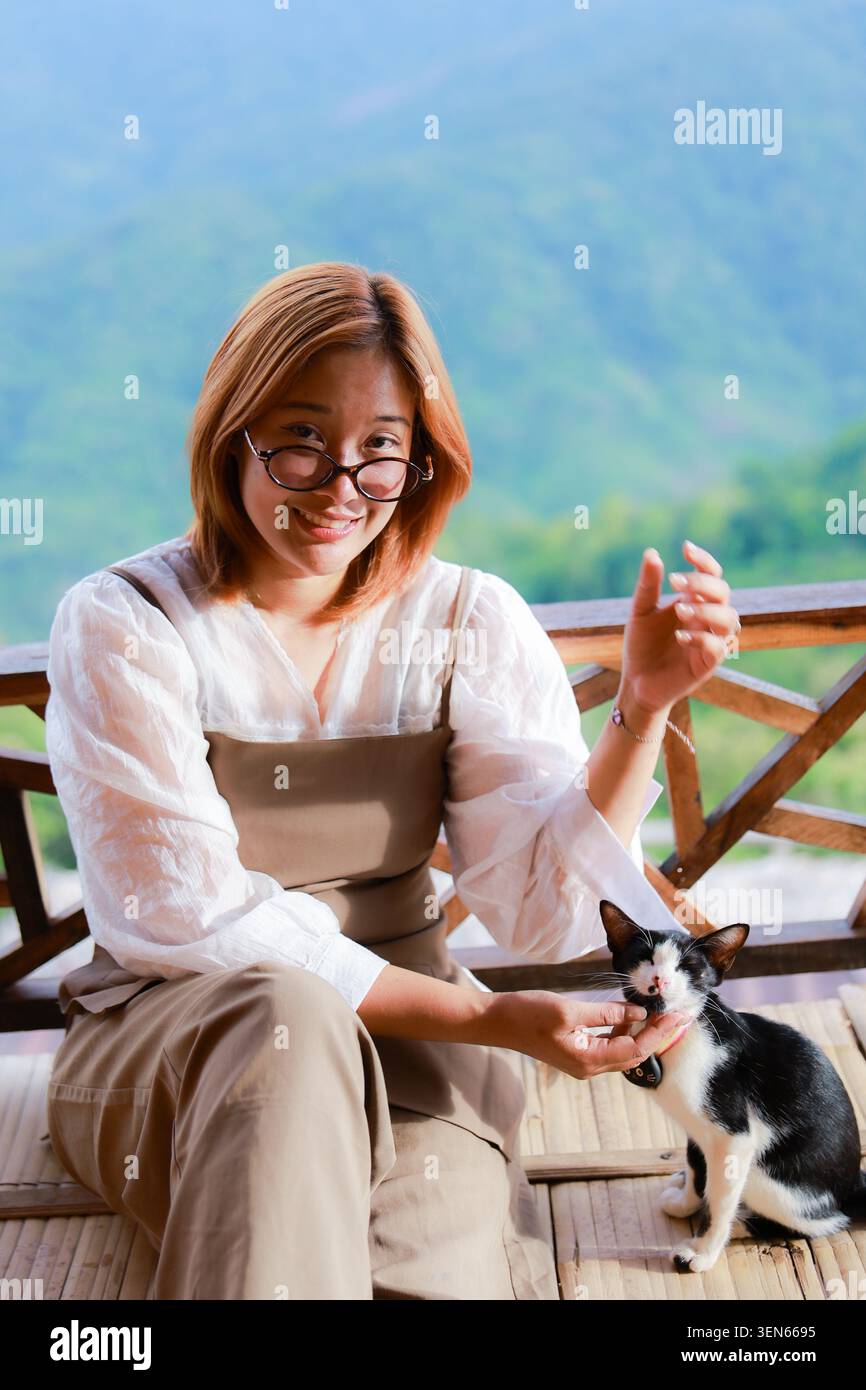 Happy Asian woman wearing eyewear sits with pet dog companion on wooden ...