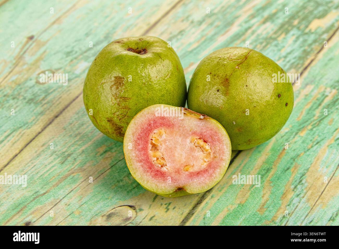 Three ripe guava fruits with green skin and vibrant pink flesh on ...