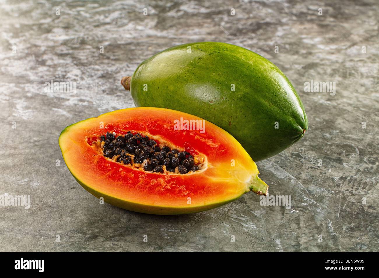 Vibrant whole green papaya and halved fruit revealing orange flesh and ...