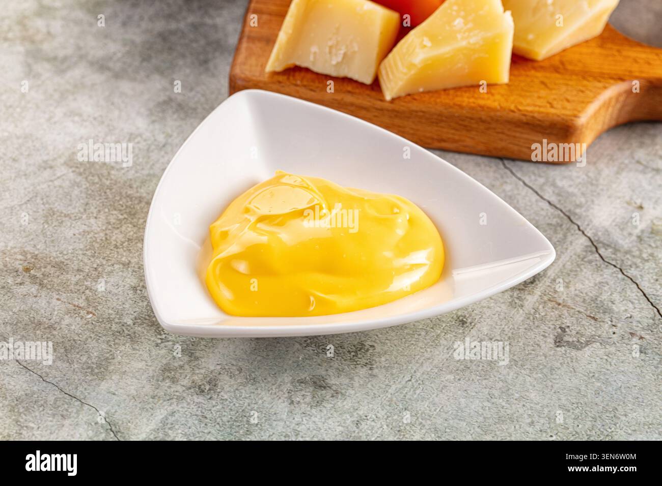 Bright yellow creamy cheese sauce in elegant white triangular bowl on ...