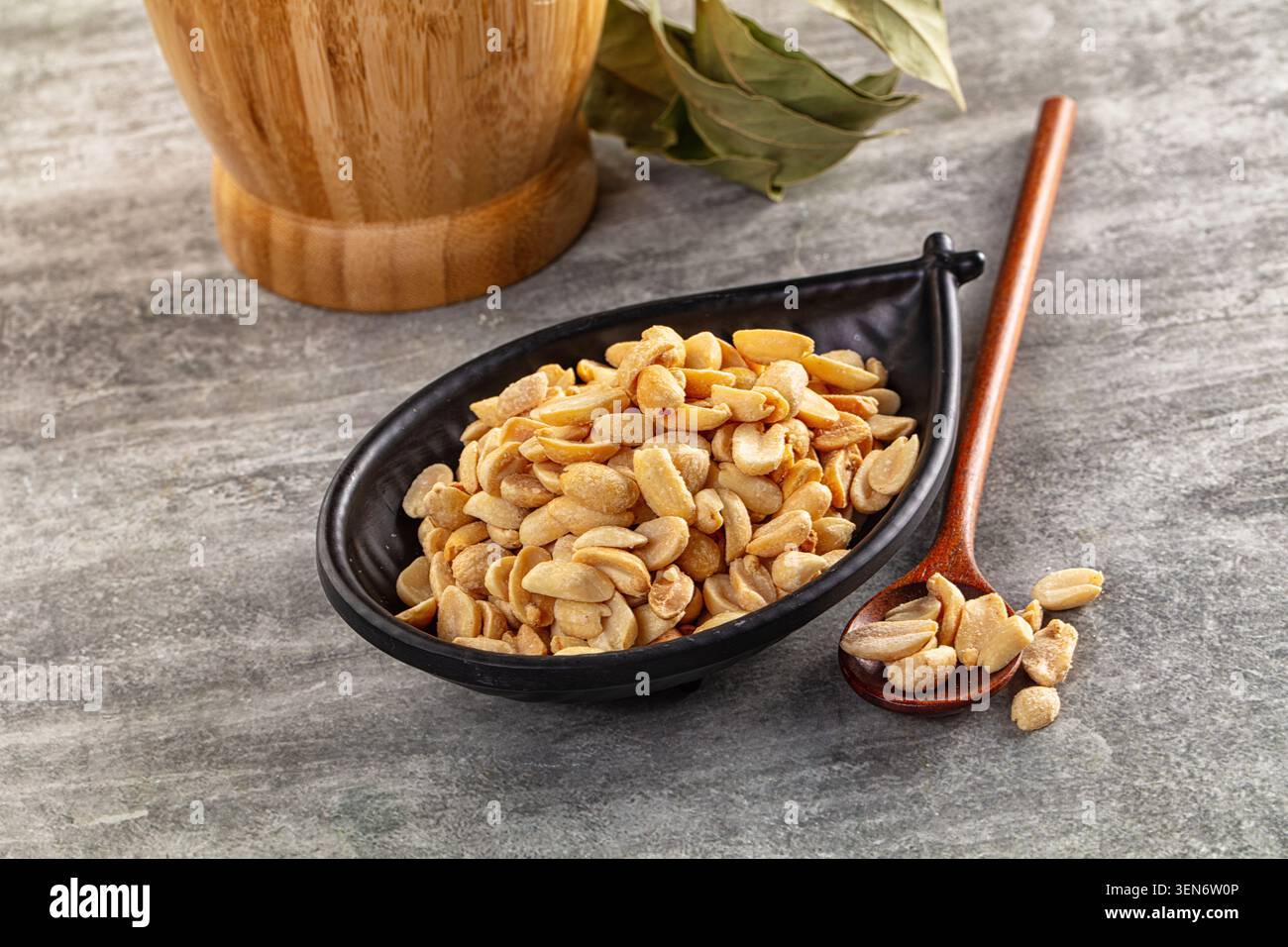 Close up of roasted peanuts in black ceramic bowl with wooden spoon and ...