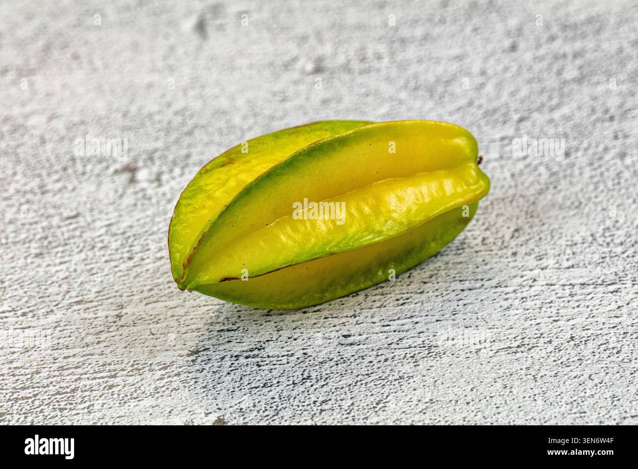 Single ripe star fruit with green and yellow skin resting on weathered ...