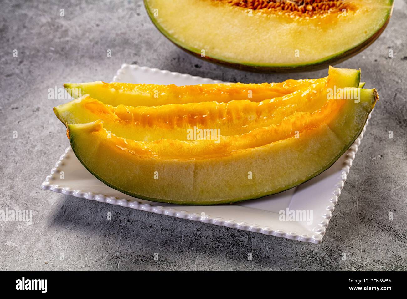 Vibrant yellow melon slices arranged on a white ceramic plate with a ...