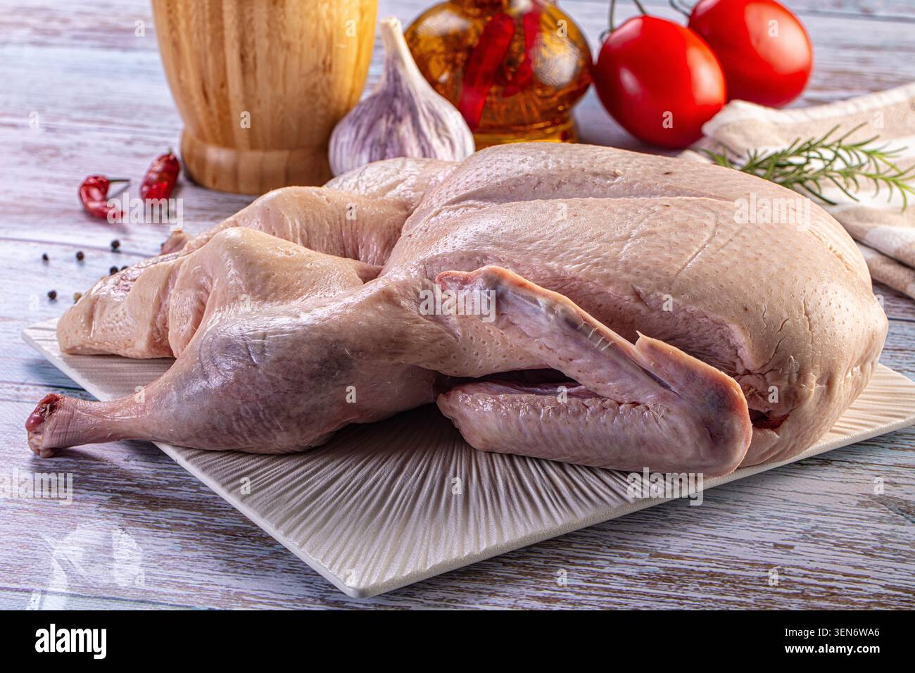 Whole raw duck on ceramic plate with garlic, tomatoes, rosemary, chili ...