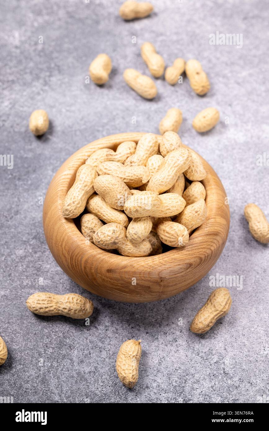 Peanuts in shell filling a round wooden bowl, scattered raw legumes ...