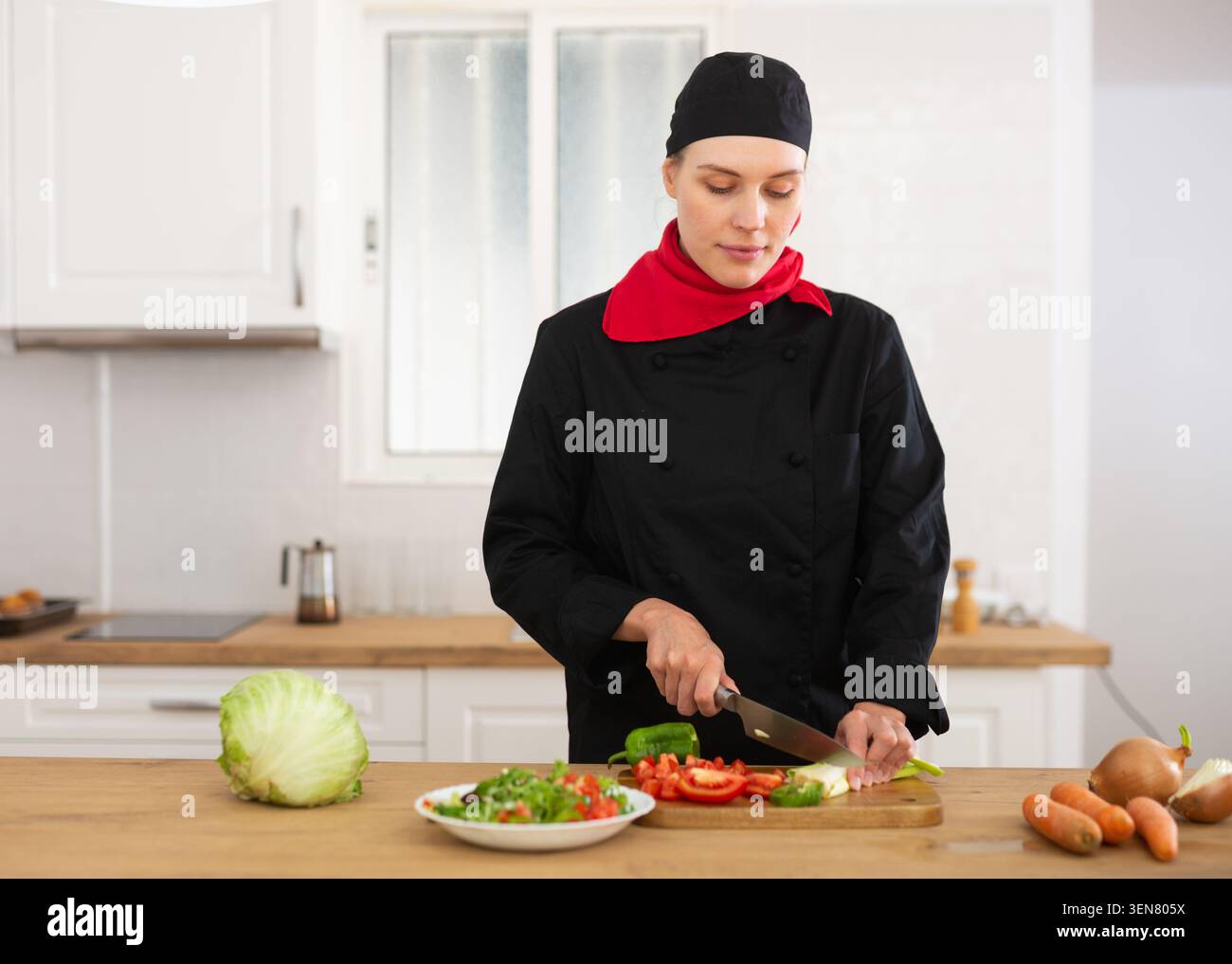 Smiling female chef in black uniform preparing vegetable salad in ...