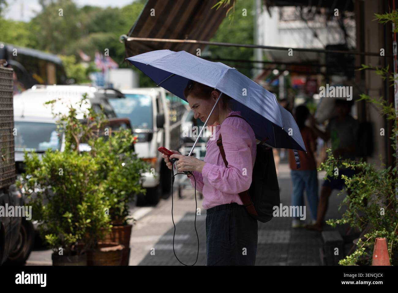 BANGKOK, THAILAND - MAY 23, 2026: Woman holding umbrella and using ...