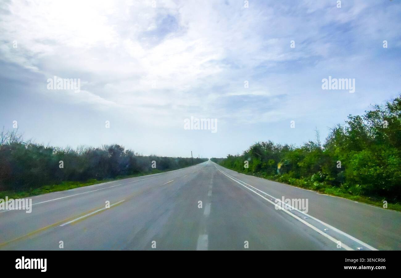 Coastal island road through rugged tropical landscape under cloudy sky ...
