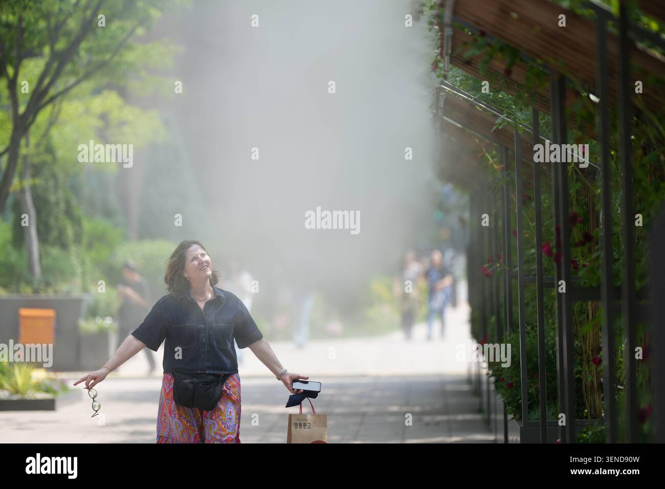 Valerie Masanet from France walks near a cooling fog device to cool ...