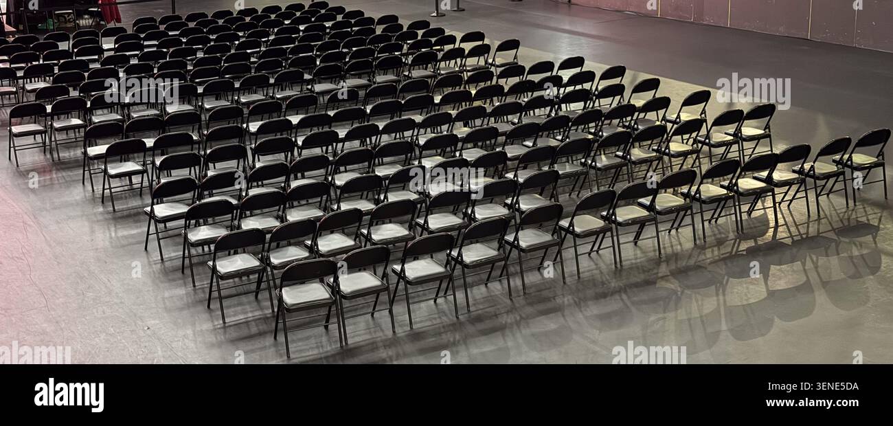 rows of empty black folding chairs in a large event hall with dark ...