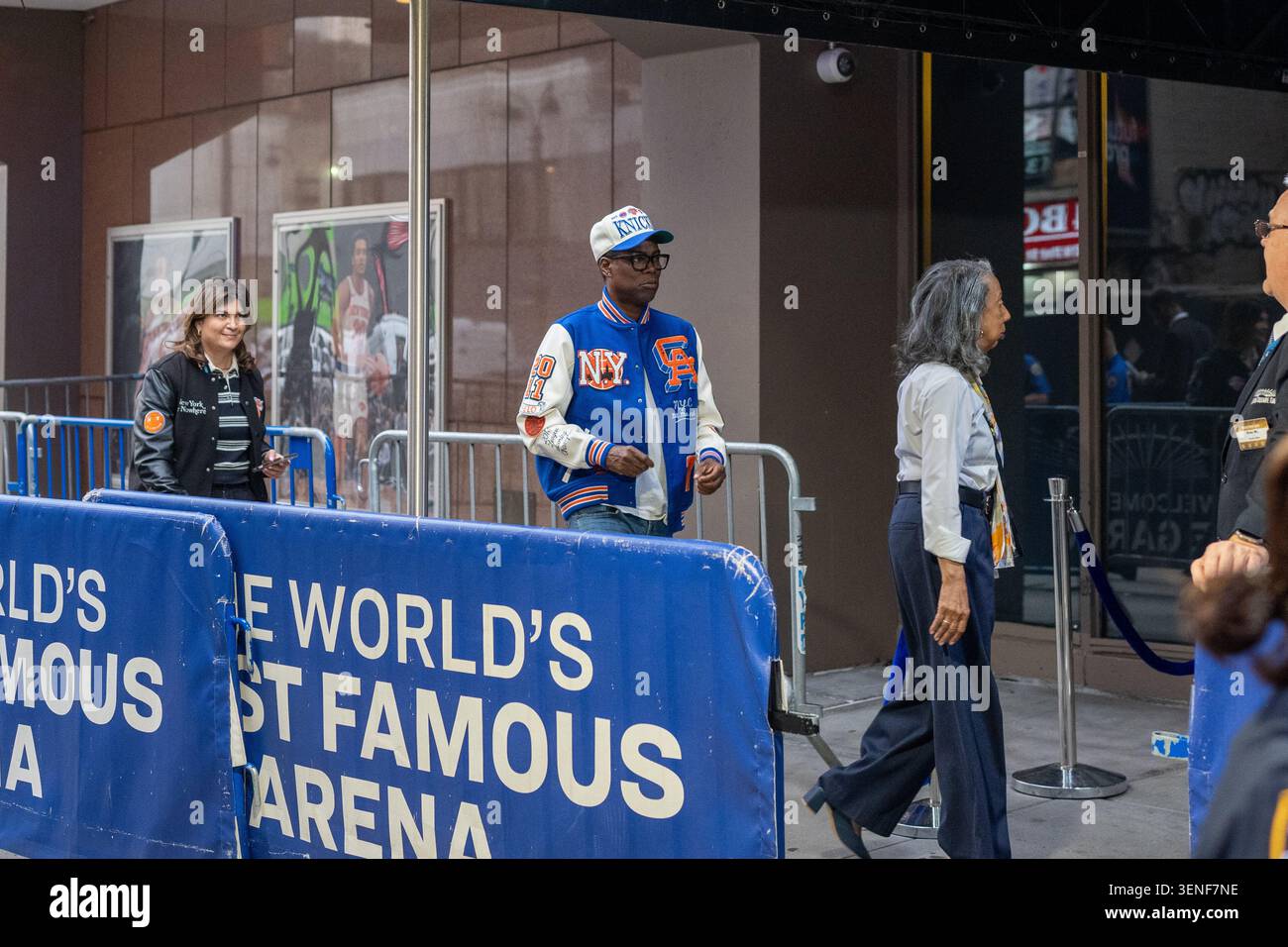 People are gathered outside an arena entrance, with a blue banner ...