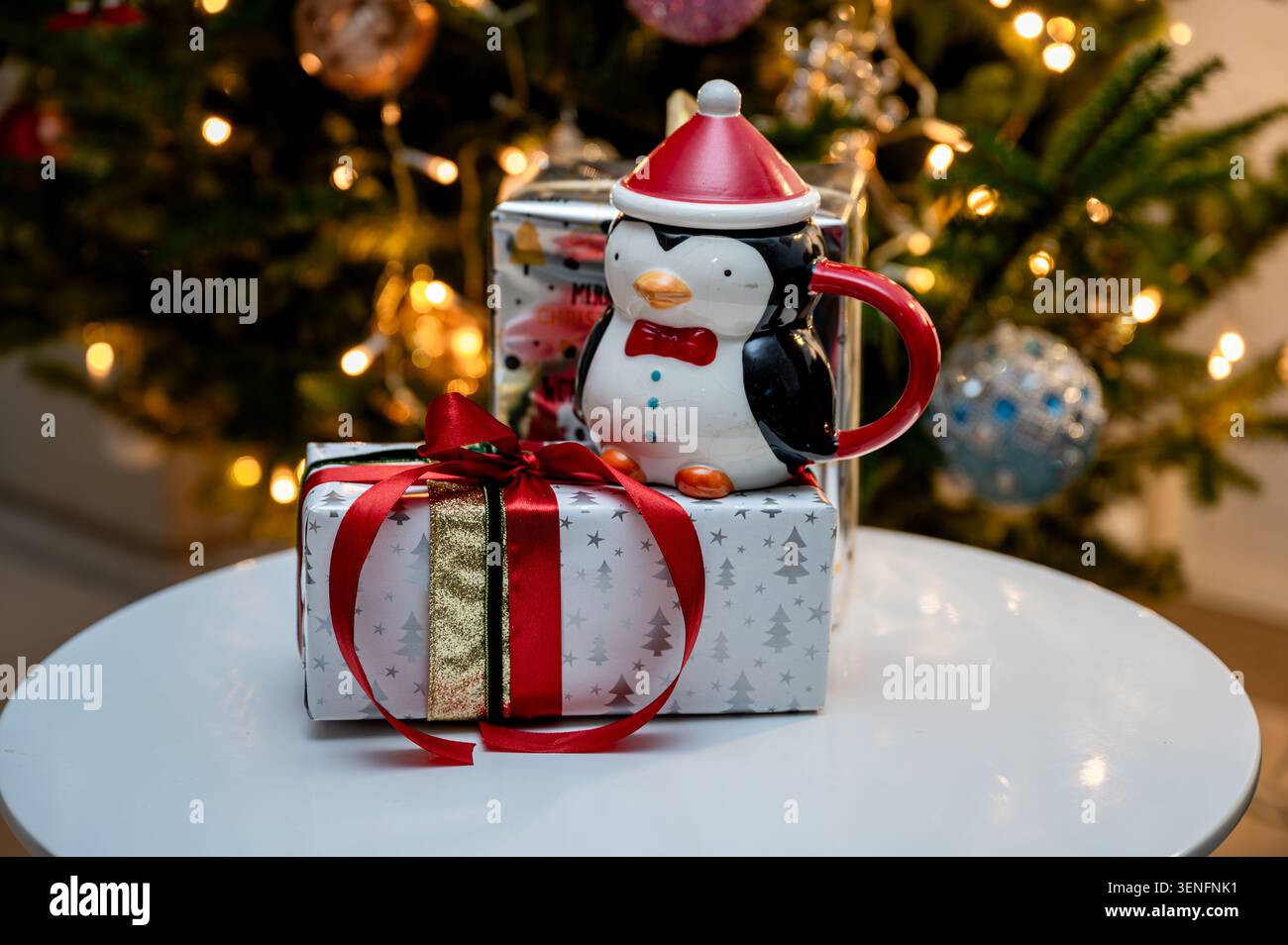 A novelty penguin mug in a Santa hat rests on a white gift box tied ...