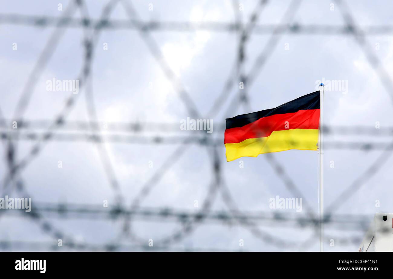 13.06.2026, Deutschland. Deutsche Flagge hinter einem Stacheldrahtzaun ...