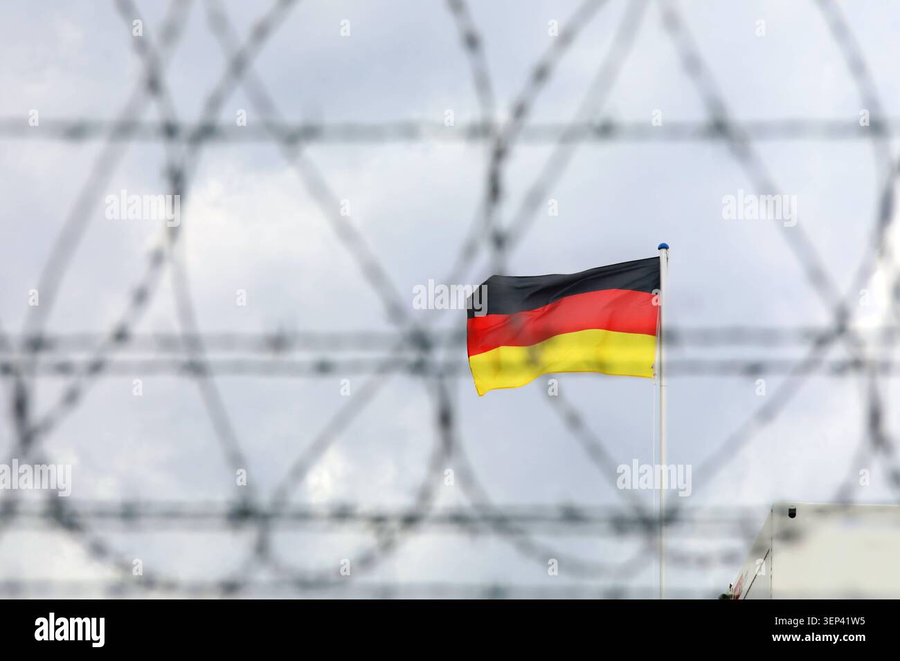 13.06.2026, Deutschland. Deutsche Flagge hinter einem Stacheldrahtzaun ...