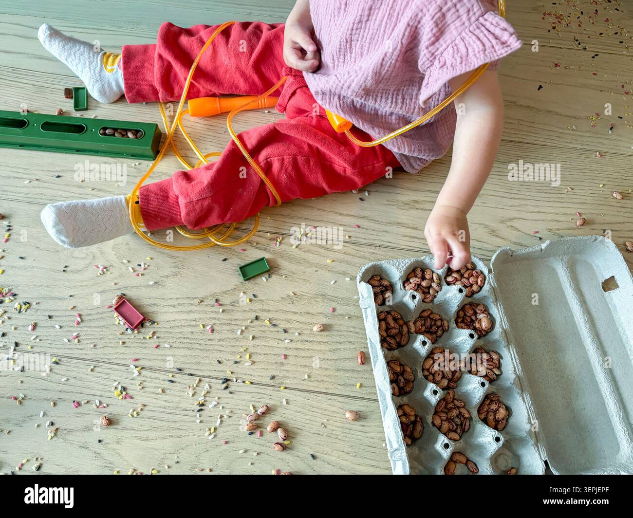 Toddler exploring sensory bin activity with beans and rice on floor ...
