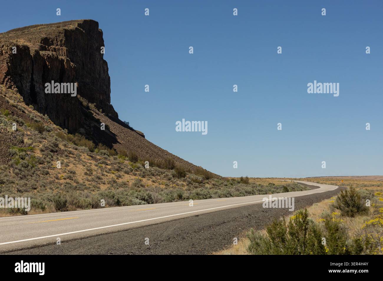 A winding highway passes beneath towering basalt cliffs in a remote ...